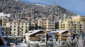 Hotel coberto de neve com vários andares, varandas e montanhas ao fundo.