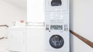 Uma lavanderia com máquinas de lavar e secar empilhadas, um painel de controle e uma pequena prateleira com objetos.
