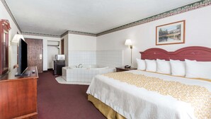 Quarto de hotel com uma cama grande, televisão, escrivaninha, banheiro com banheira e um quadro na parede.