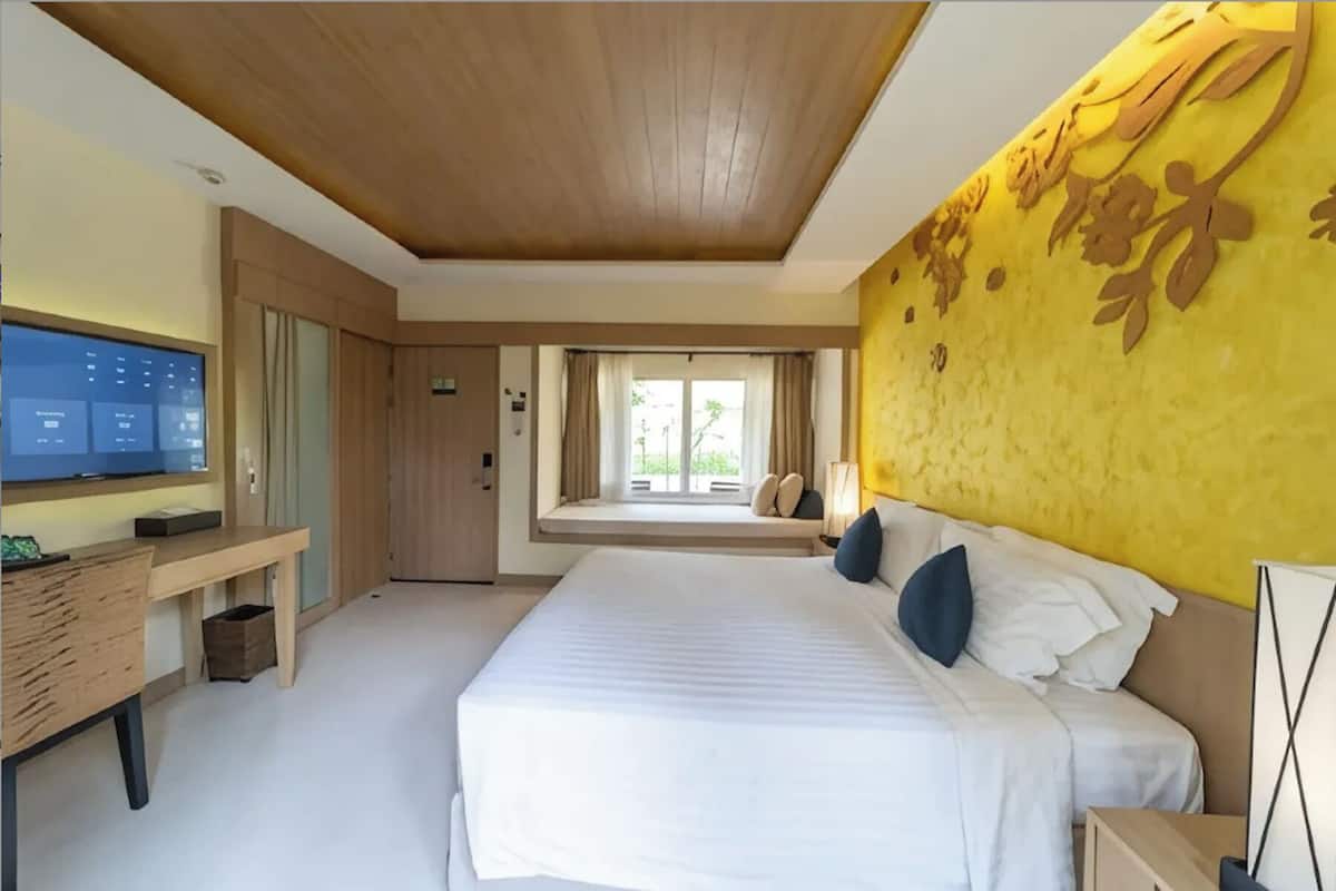 Quarto de hotel com uma cama grande, uma mesa de escritório, televisão e janela com vista para vegetação.