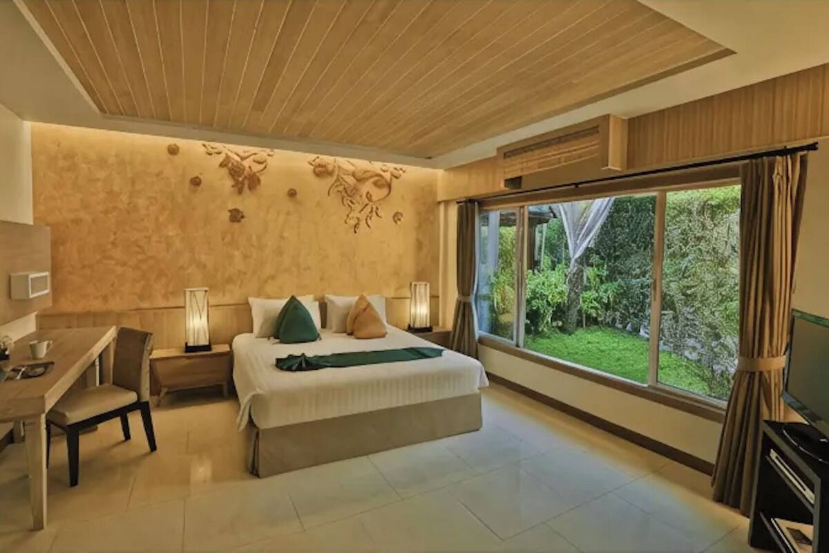 Quarto com cama, mesas de cabeceira, escrivaninha e televisão.