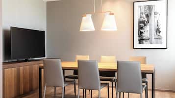 Uma área de jantar moderna com mesa de madeira, seis cadeiras, televisão de tela plana e iluminação pendente.