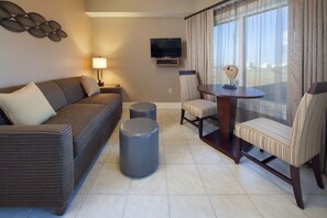 Uma sala de estar moderna com um sofá, dois pufes, uma poltrona listrada, uma mesa e uma TV fixada na parede.