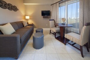 Uma sala de estar moderna com um sofá, dois pufes, uma poltrona listrada, uma mesa e uma TV fixada na parede.