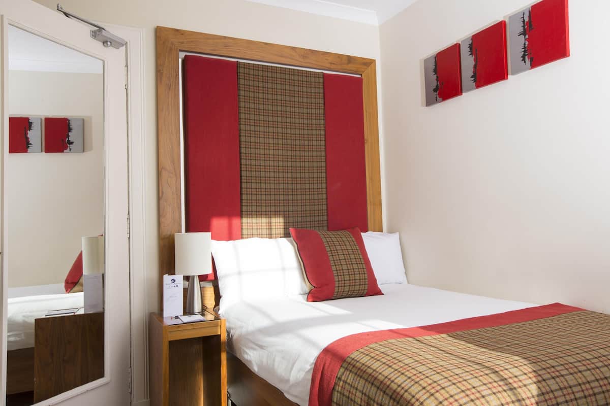 Quarto de hotel com cama, mesa de cabeceira, espelho e porta.