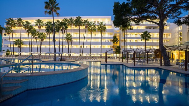 Um hotel com piscina, palmeiras e fachada de prédio bem iluminada.
