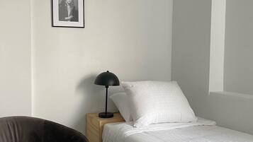 Um quarto com uma cama, uma cadeira, uma mesinha de cabeceira, uma luminária e um quadro na parede.