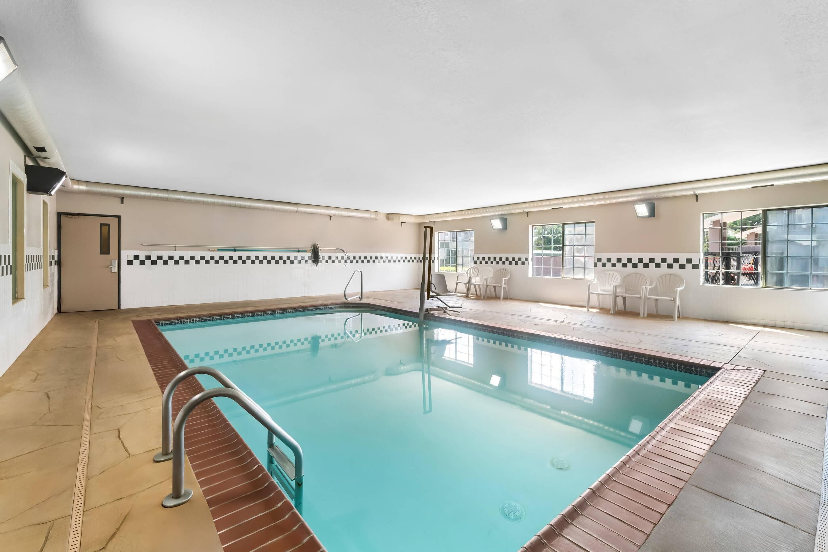 Uma piscina com borda xadrez, escada e deck revestido de azulejos.