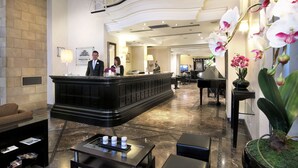 Um saguão de hotel com balcão de recepção, um piano e uma orquídea em vaso grande.