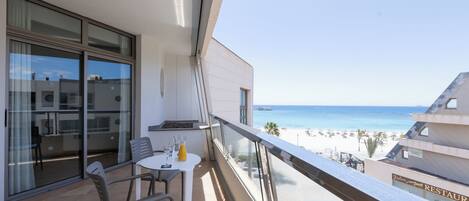 Varanda com mesa e cadeiras, vista para a praia e um restaurante.