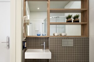 Casa de banho com lavatório branco, espelho e estante de madeira com plantas.