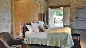 Quarto com cama, cadeira, banco e parede de pedra.
