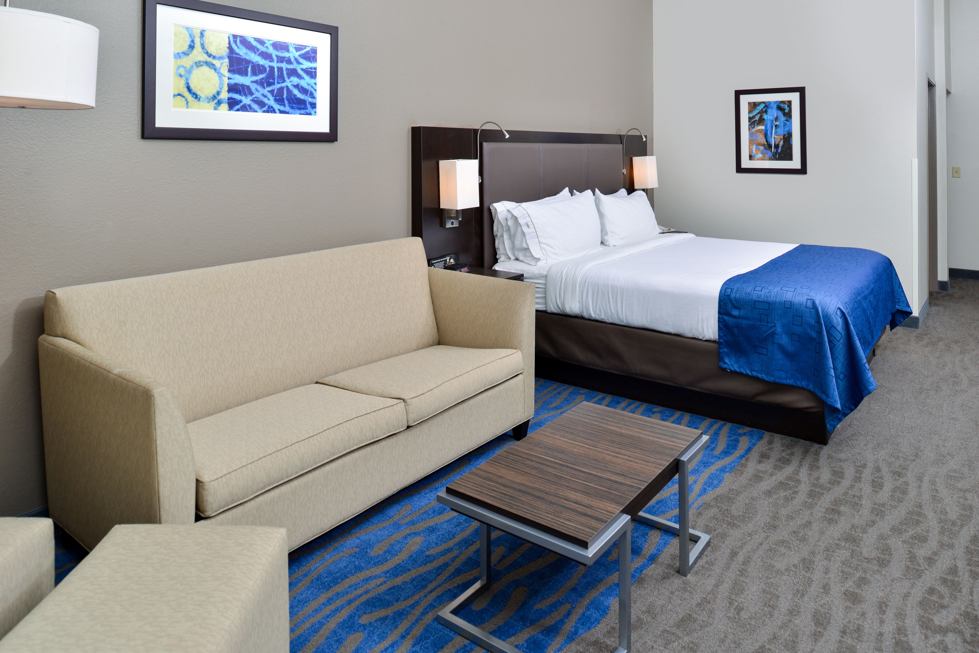Quarto de hotel com cama, sofá, mesa pequena e duas luminárias fixadas na parede.