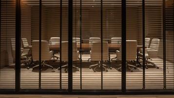 Uma sala de conferência com design moderno, apresentando uma mesa comprida rodeada por cadeiras e um painel de vidro.