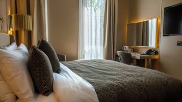 Quarto de hotel com uma cama grande, uma escrivaninha com cadeira, televisão e janela com cortinas.