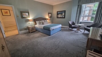 Quarto com cama, mesas de cabeceira, uma cadeira e uma mesinha.