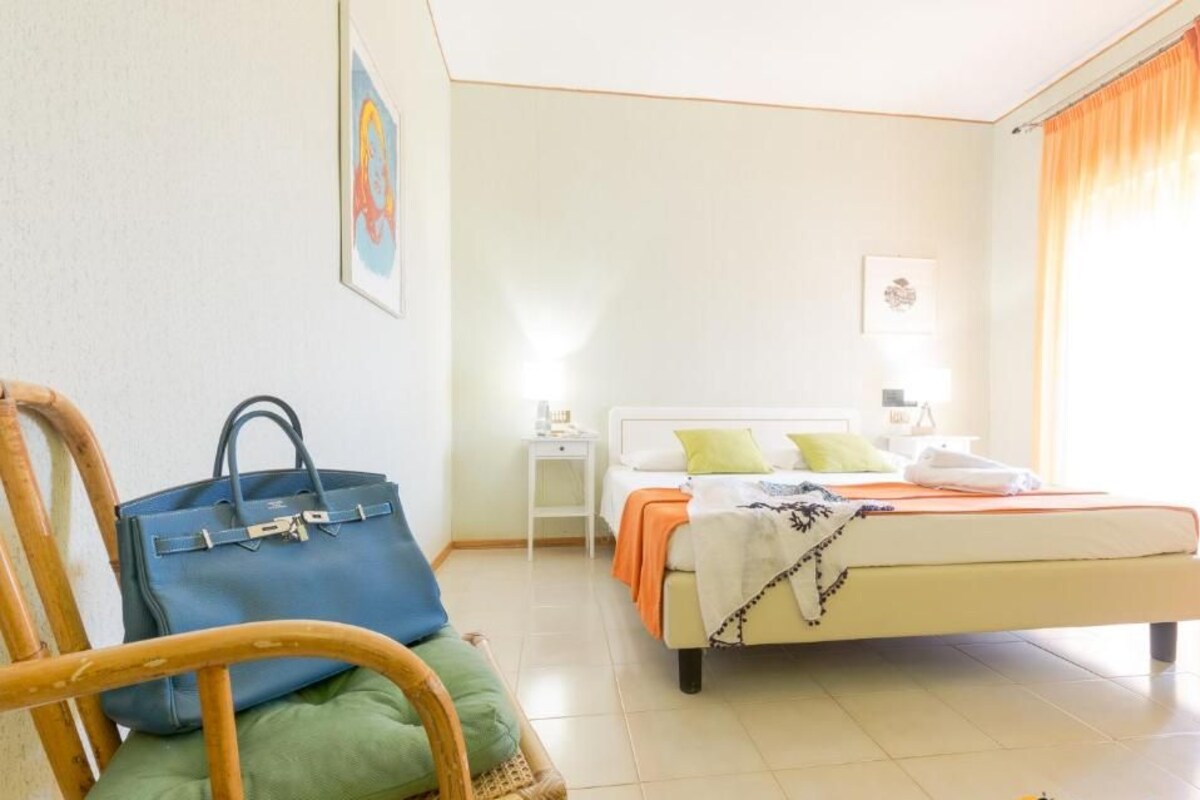 Quarto de hotel com cama, uma cadeira, mesa de cabeceira, luminária e um quadro na parede.