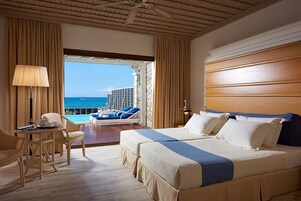 Quarto de hotel com cama, escrivaninha, cadeira e vista para a piscina e oceano.