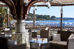 Um alpendre à beira-mar com móveis de vime, uma mesa de vidro e vista para a praia e o oceano.
