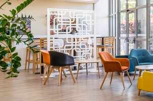 Espaço moderno e interno com piso de madeira, divisória decorativa branca e diversas áreas de estar, incluindo cadeiras laranja e azuis.