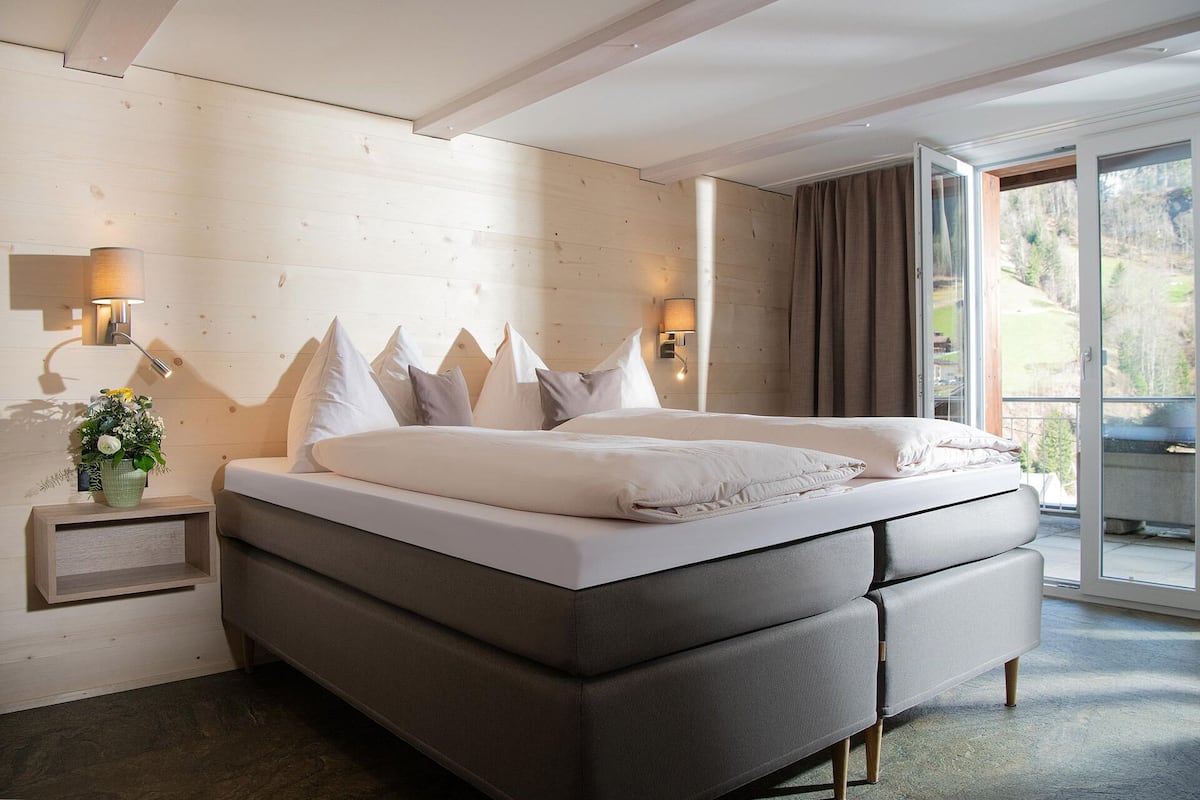 Quarto moderno com uma cama grande, mesa de cabeceira com abajur e vista para o exterior.