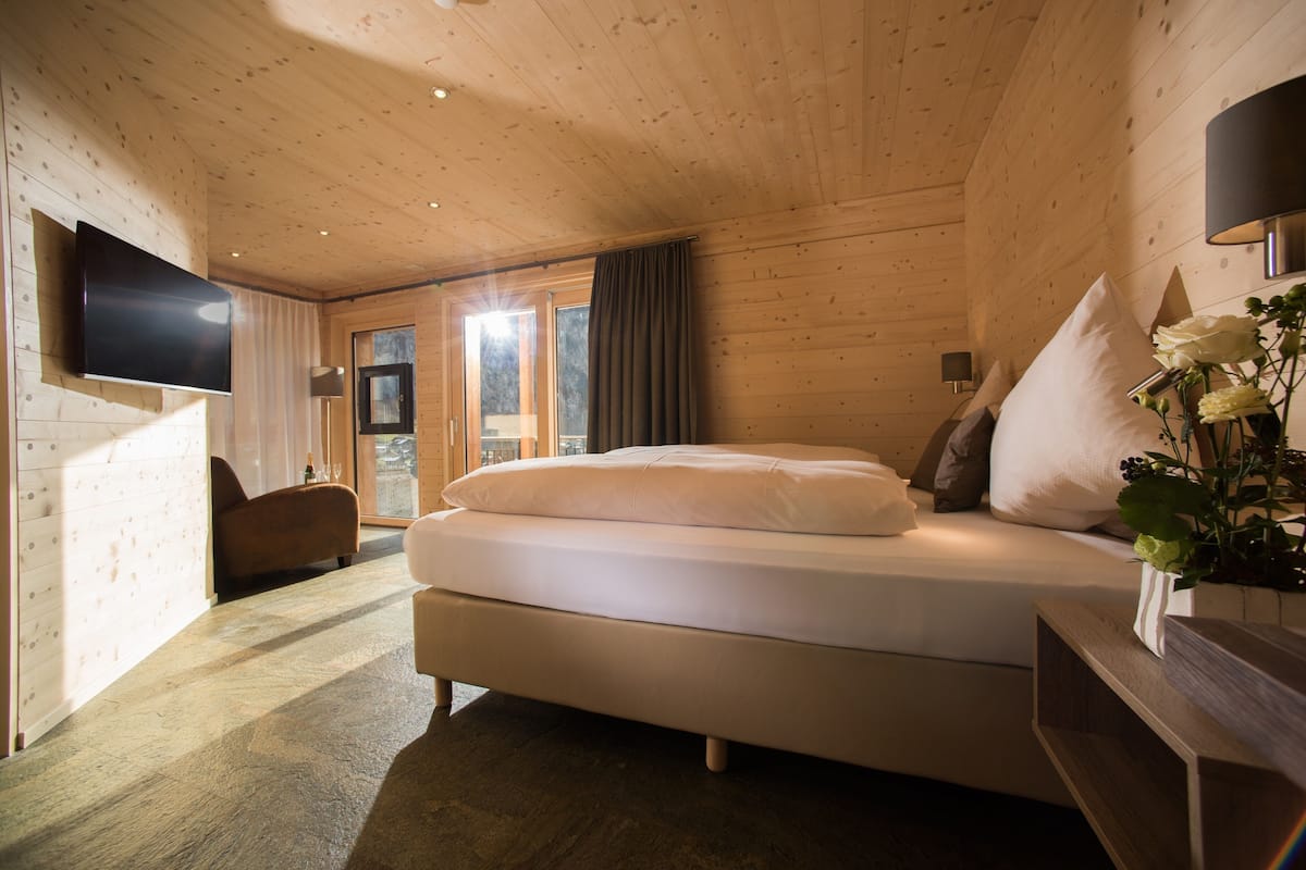 Quarto com cama grande, paredes de madeira, televisão de tela plana e janela com cortinas.