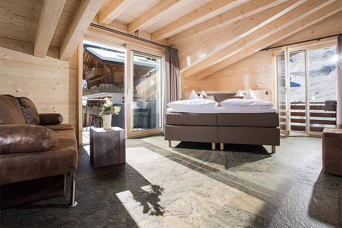 Um quarto aconchegante com uma cama grande, teto de madeira e uma porta de vidro deslizante que dá para uma varanda.