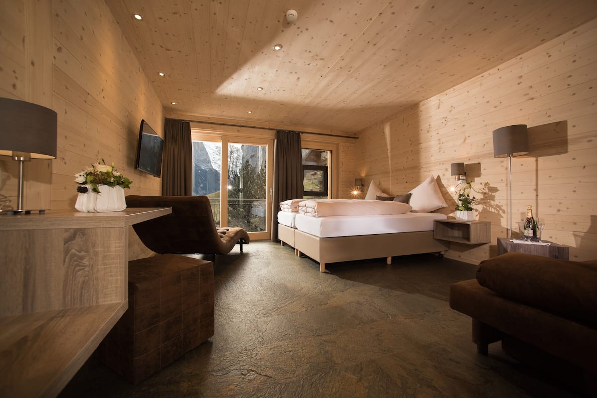 Quarto moderno com teto de madeira, uma cama grande, um sofá e uma escrivaninha com abajur.