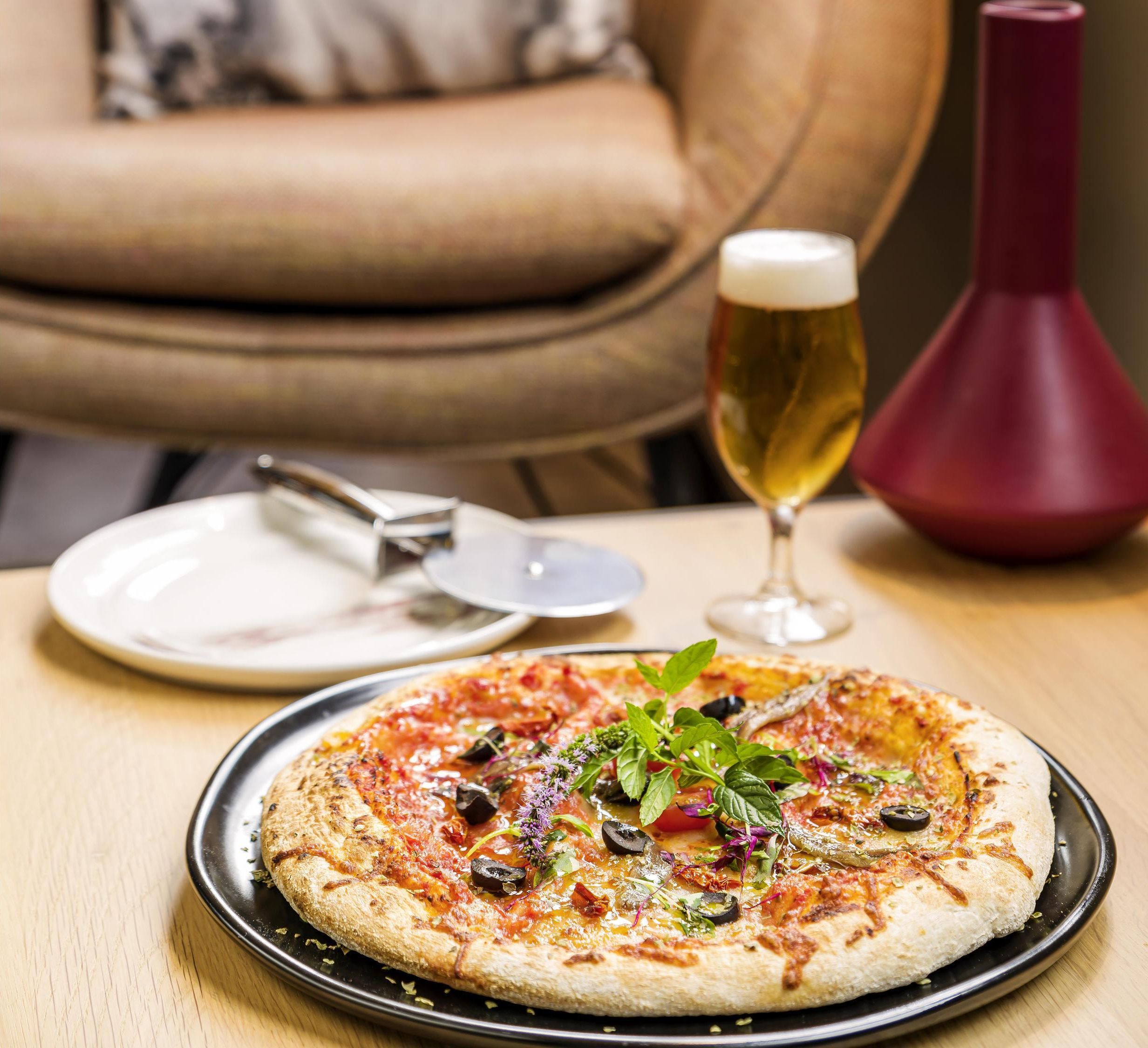 Pizza num prato, com um copo de cerveja e um vaso vermelho ao fundo.