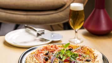 Pizza num prato, com um copo de cerveja e um vaso vermelho ao fundo.