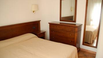 Quarto com cama de madeira, cômoda, mesa de cabeceira, luminária na parede e espelho.