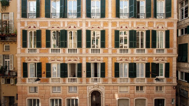 Um edifício com vários andares e detalhes arquitetônicos elaborados, incluindo molduras e venezianas decorativas, varandas e uma entrada central com arco.