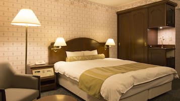 Quarto de hotel com cama, duas luminárias de cabeceira, mesa de cabeceira com telefone, uma cadeira e uma mesinha.