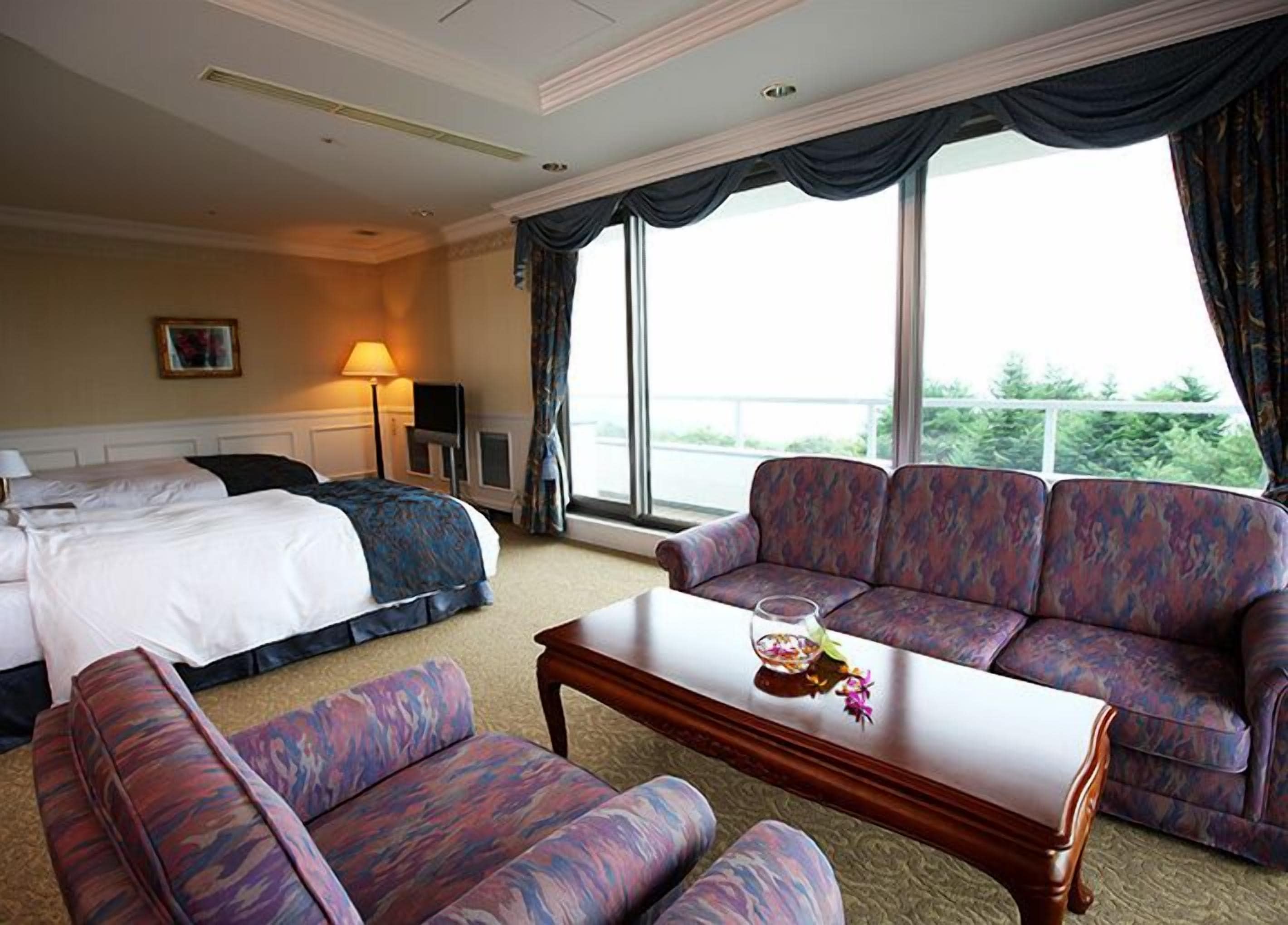 Quarto de hotel com cama, sofá, mesa de centro e televisão.
