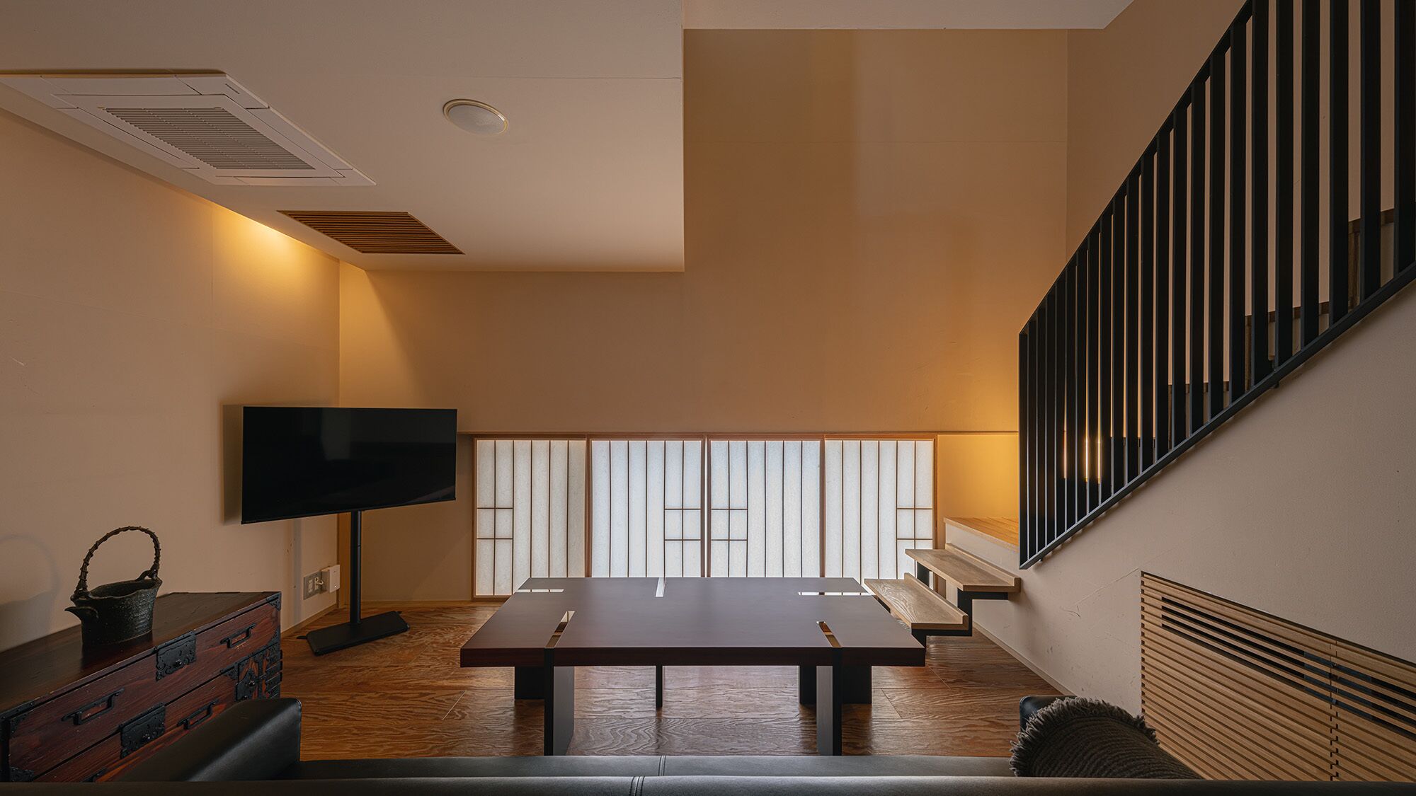 Um interior moderno com uma TV de tela plana, uma mesa de madeira e uma escada com corrimãos pretos.