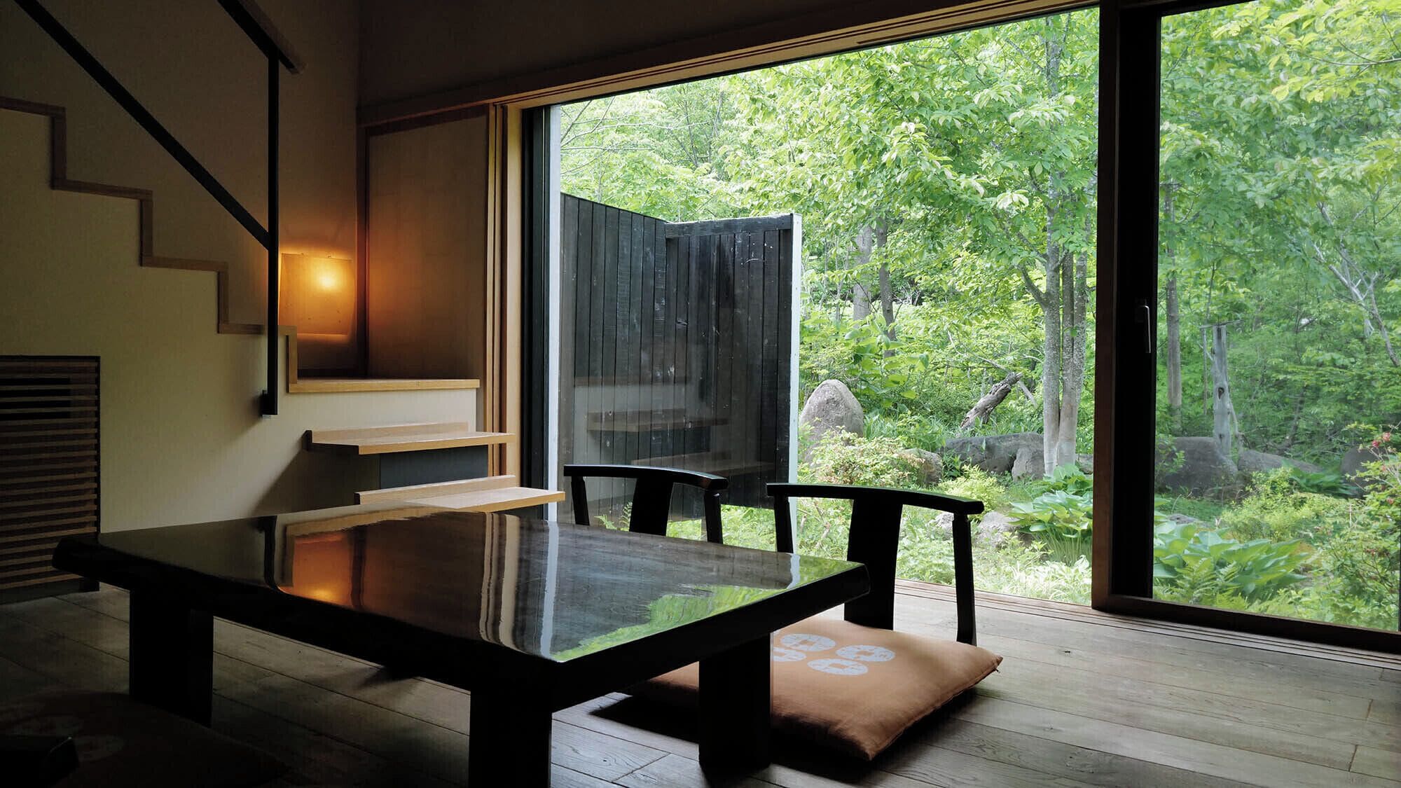 Interior moderno com uma mesa de madeira, cadeiras, uma escada e uma janela grande com vista para uma floresta.