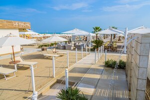 Um café à beira-mar com mesas ao ar livre, guarda-sóis e vista para o mar.