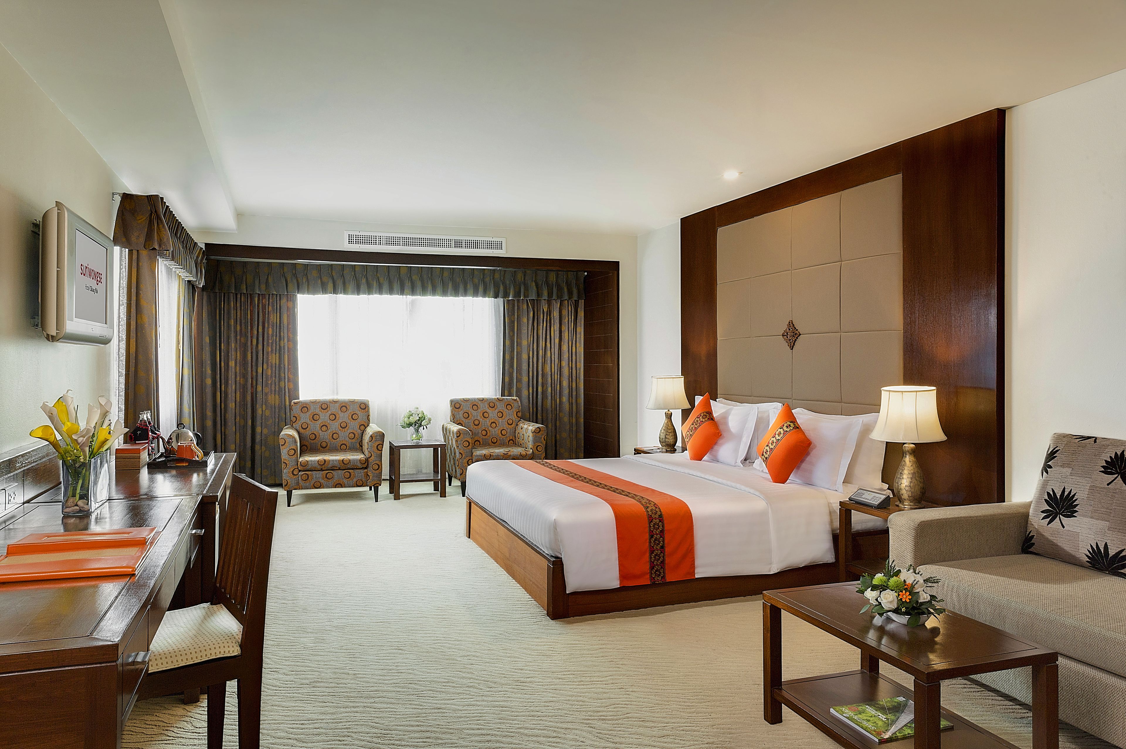 Quarto de hotel com uma cama grande, um sofá, uma escrivaninha e duas poltronas.