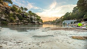 Uma praia com costa rochosa, mar calmo e edifícios ao fundo.