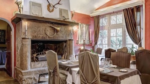 Uma sala de jantar com lareira de pedra, cadeiras de madeira e uma mesa posta para refeição.