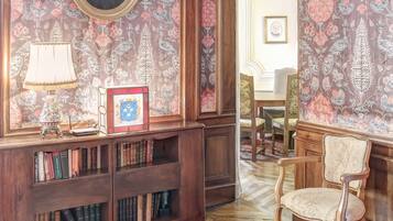 Quarto com piso de madeira em padrão herringbone, uma estante de madeira, um retrato emoldurado e papel de parede estampado.
