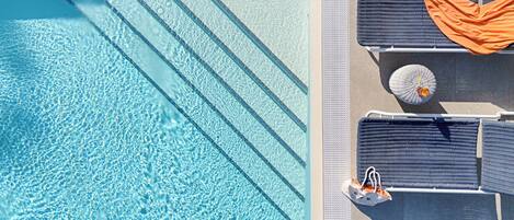 Vista aérea de uma piscina com água cristalina, cadeiras de descanso próximas e um caminho com textura.