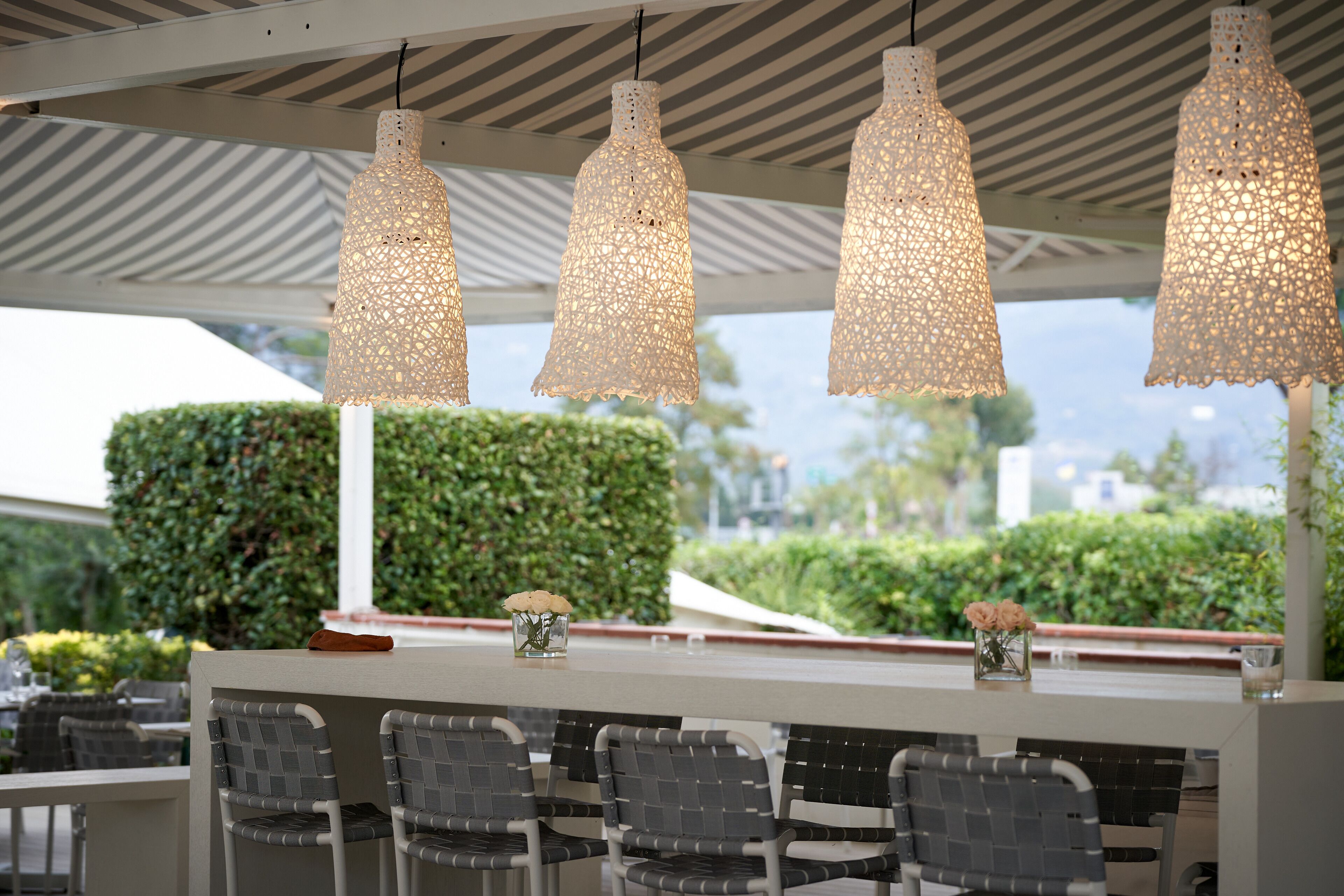 Uma área de bar com quatro luminárias pendentes, uma mesa branca e várias cadeiras.