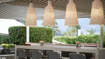 Uma área de bar com quatro luminárias pendentes, uma mesa branca e várias cadeiras.