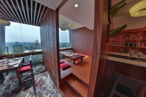 Uma área de refeições moderna com vista para a cidade, móveis de madeira e um bar com copos.