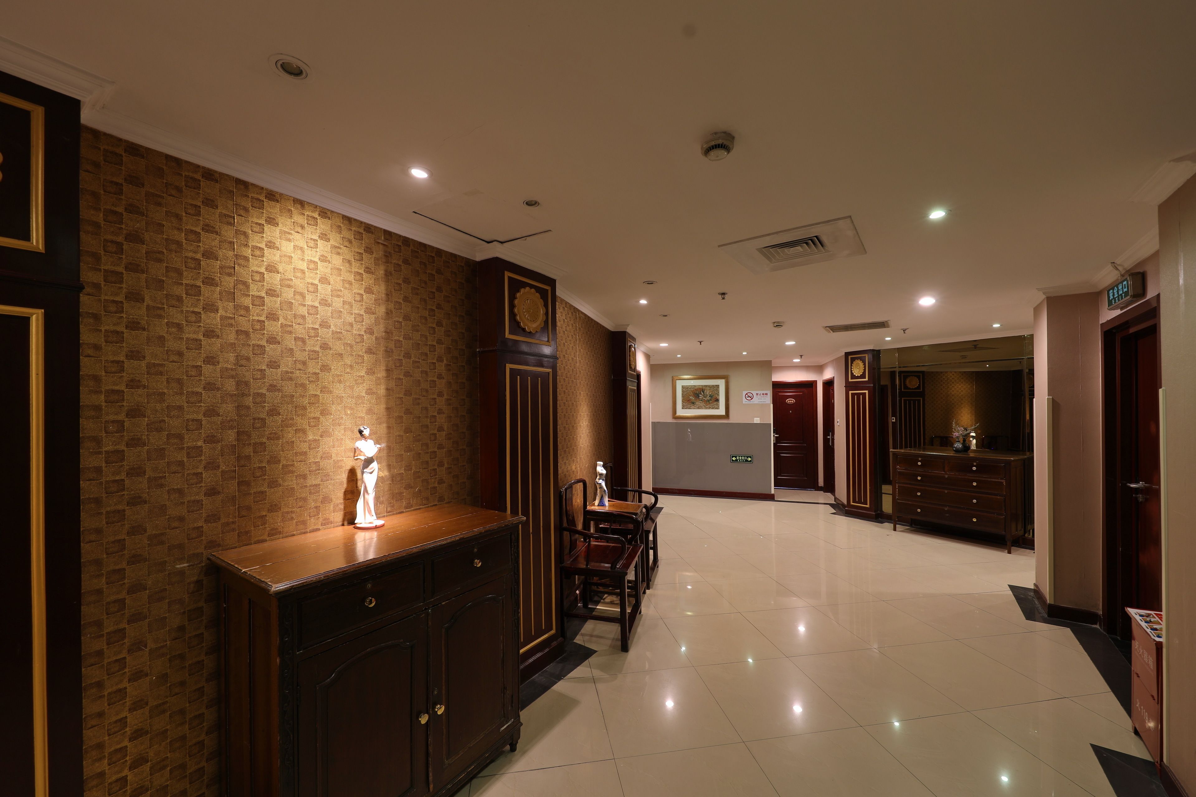 Um saguão de hotel com balcão de recepção, cadeiras de madeira, um relógio e piso de azulejos.