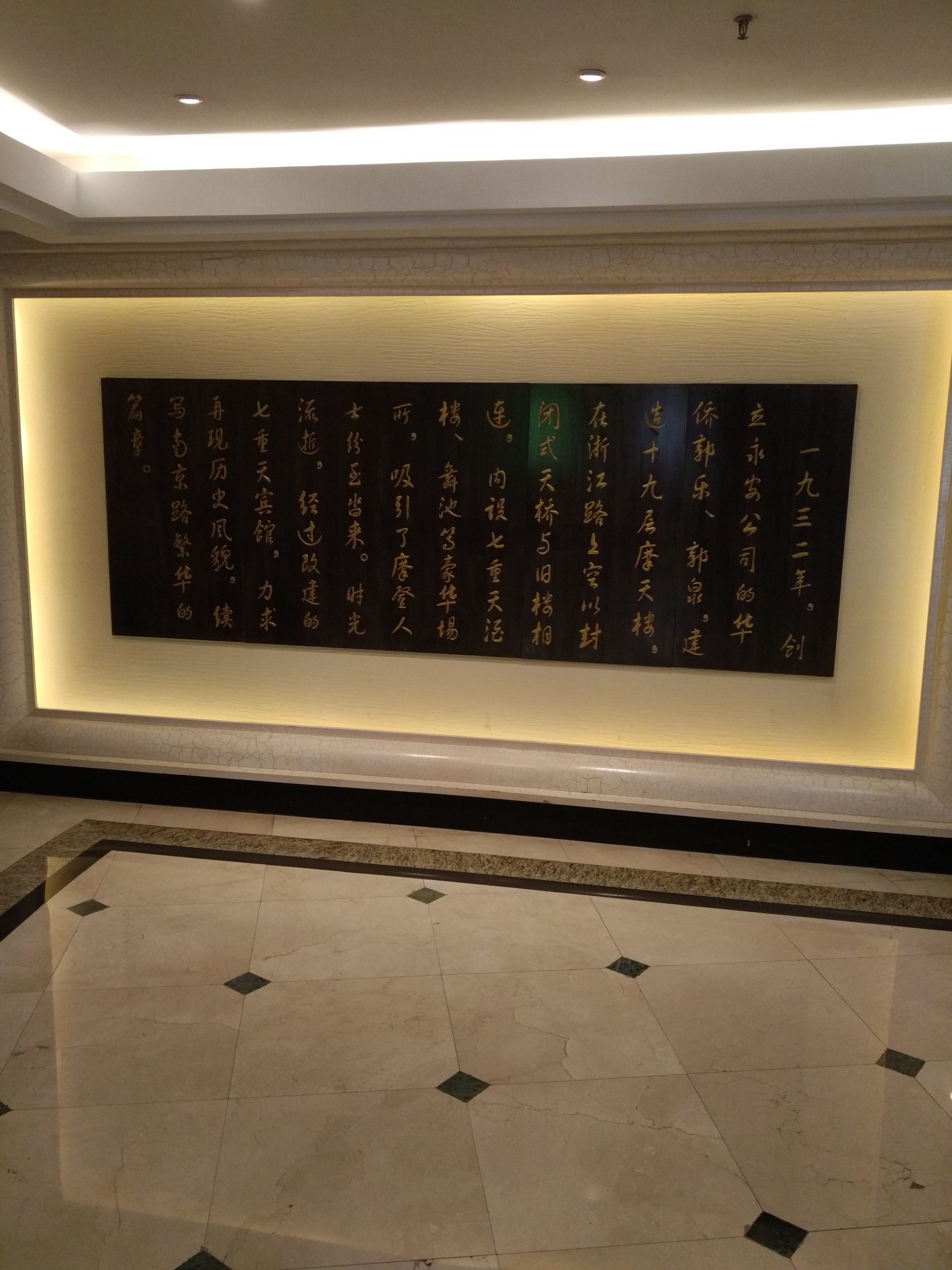 Um corredor com uma placa preta grande com caracteres chineses dourados, piso de azulejos e iluminação embutida no teto.