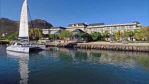 Um veleiro atracado perto de um hotel à beira-mar, com montanhas ao fundo.