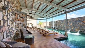 Uma área de piscina descoberta coberta, com espreguiçadeiras, um muro de pedra e um deck de madeira.