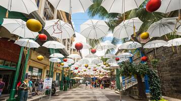 Rua de pedestres com guarda-sóis brancos pendurados, palmeiras e um pinheiro de Natal.